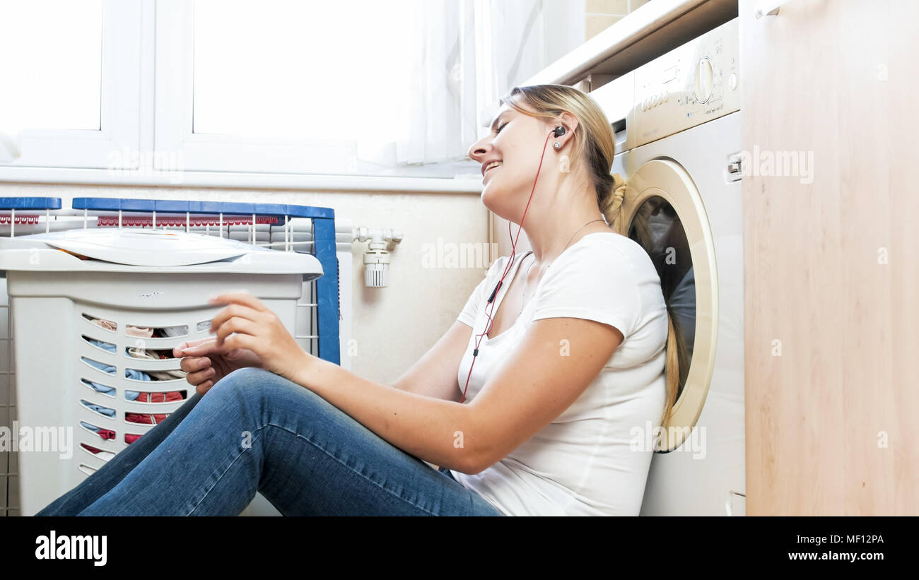 Portrait of young smiling woman sitting on floor at laundry and ...