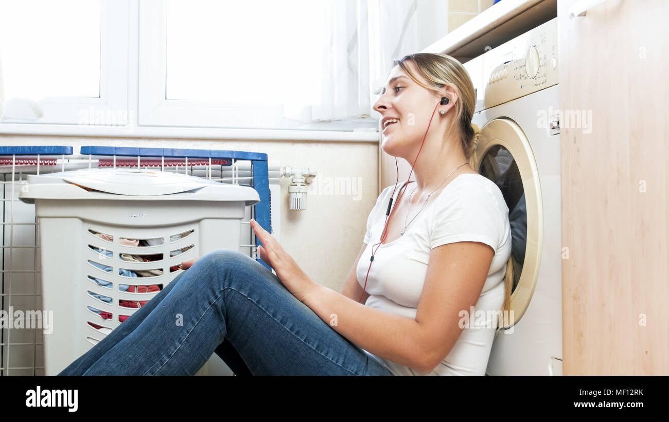 Portrait of smiling young housewife singing and listening to music at ...