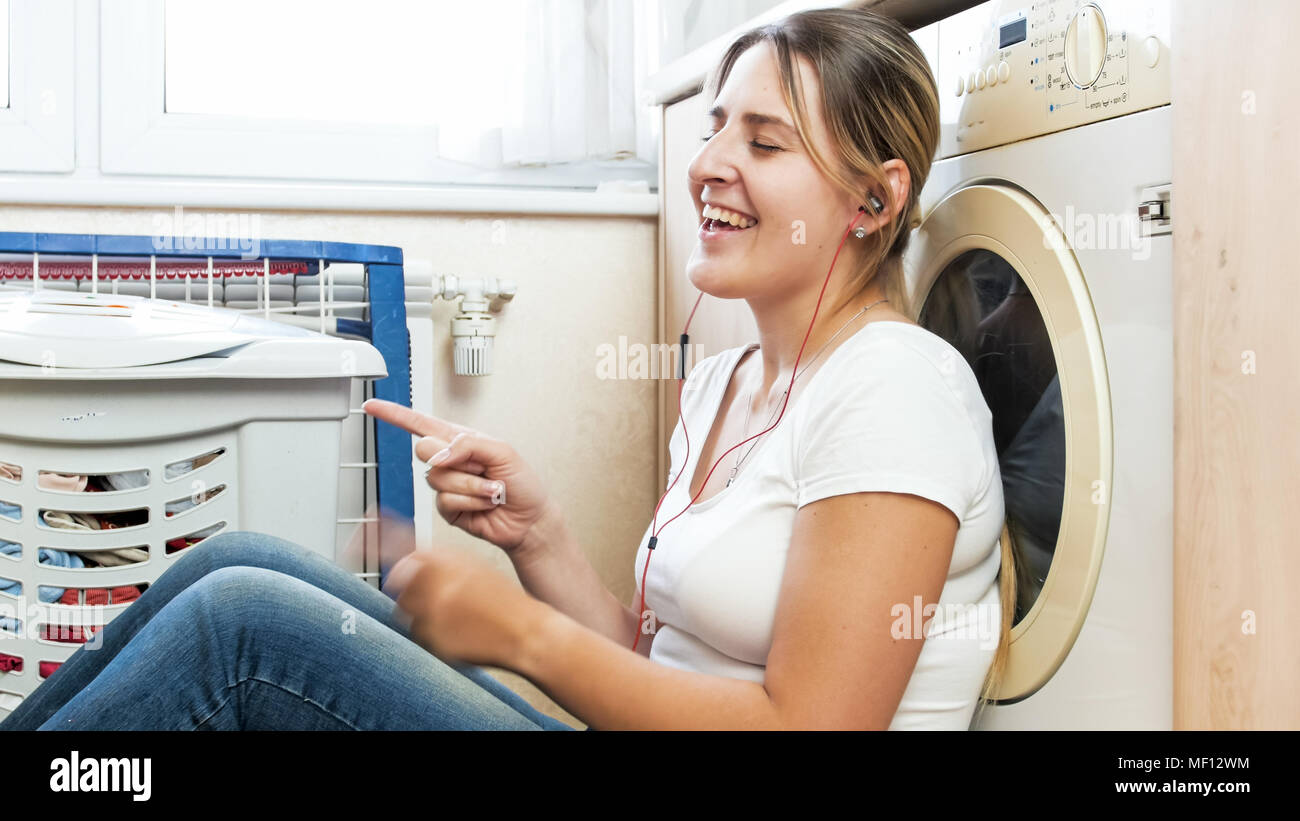 Beautiful smiling woman singing and listening music on floor at laundry ...