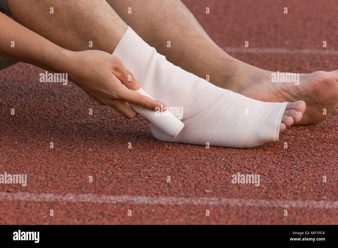 Male athlete applying compression bandage onto ankle injury of a ...
