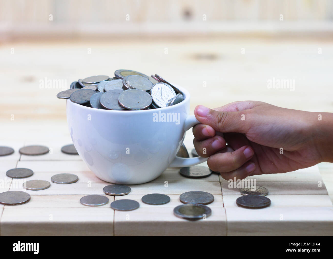 The coin in a white coffee cup rests on a wooden table and around a cup ...