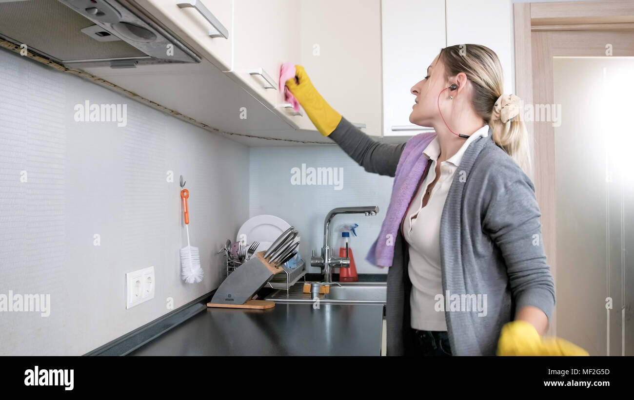Beautiful young housewife listening music with earphones while doing ...