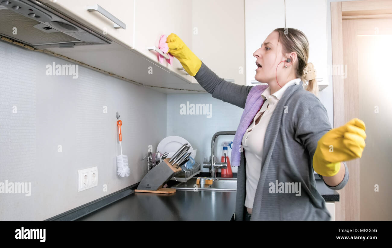 Portrait of singing young woman listening music and doing housework ...