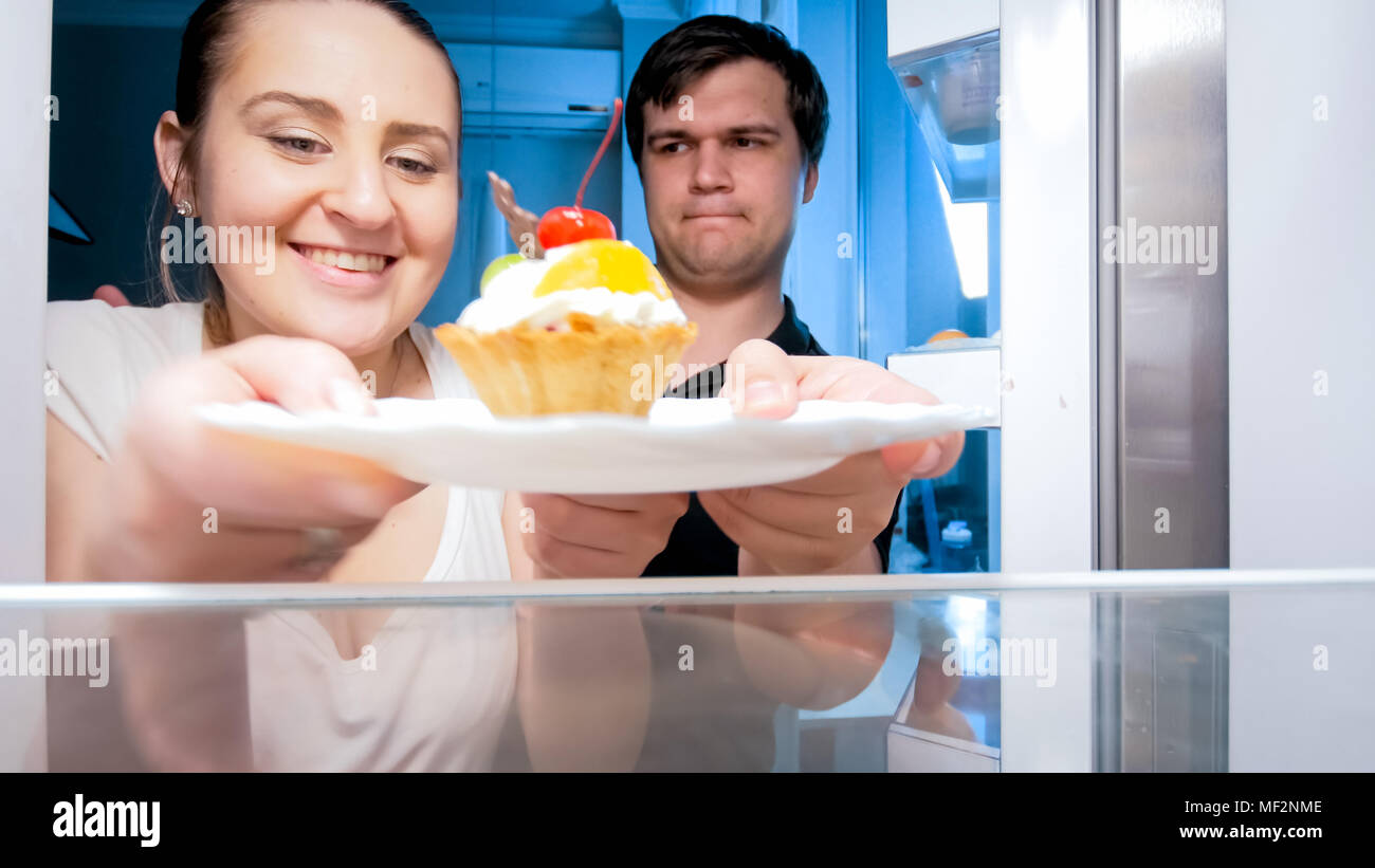 Portrait of hungry young couple fighting for piece of cake at night ...