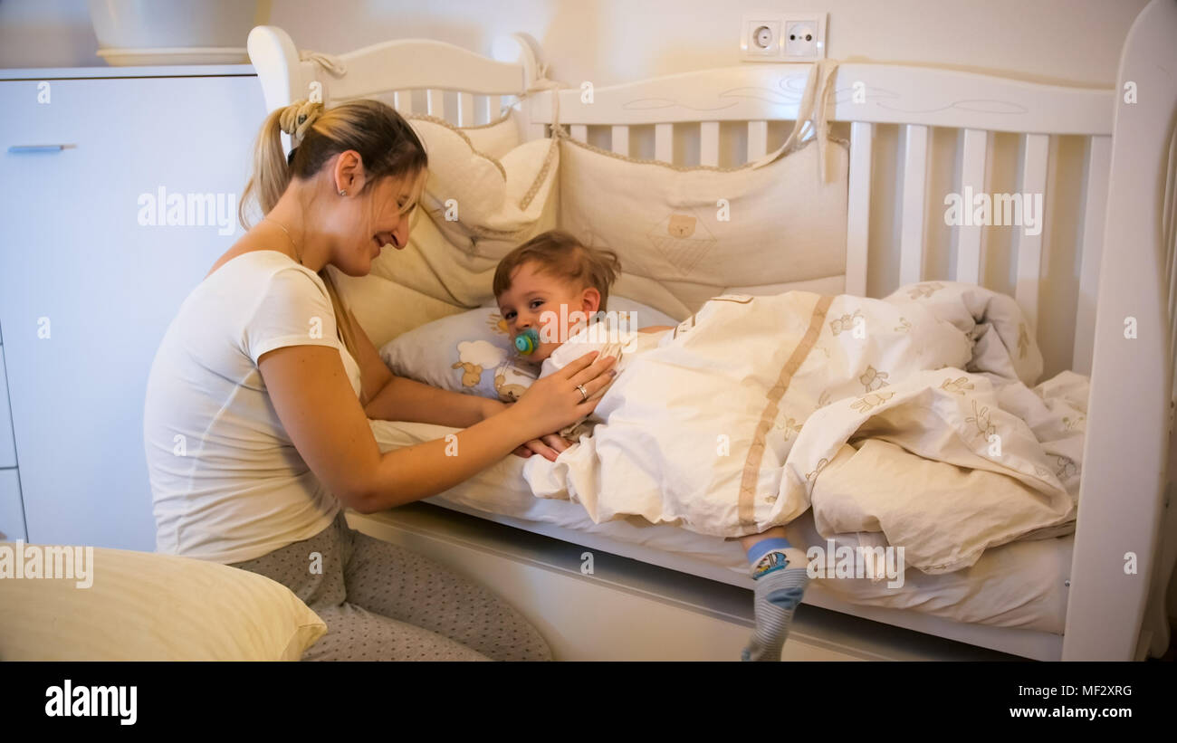 Young mother caressing her crying toddler son lying in bed at night ...