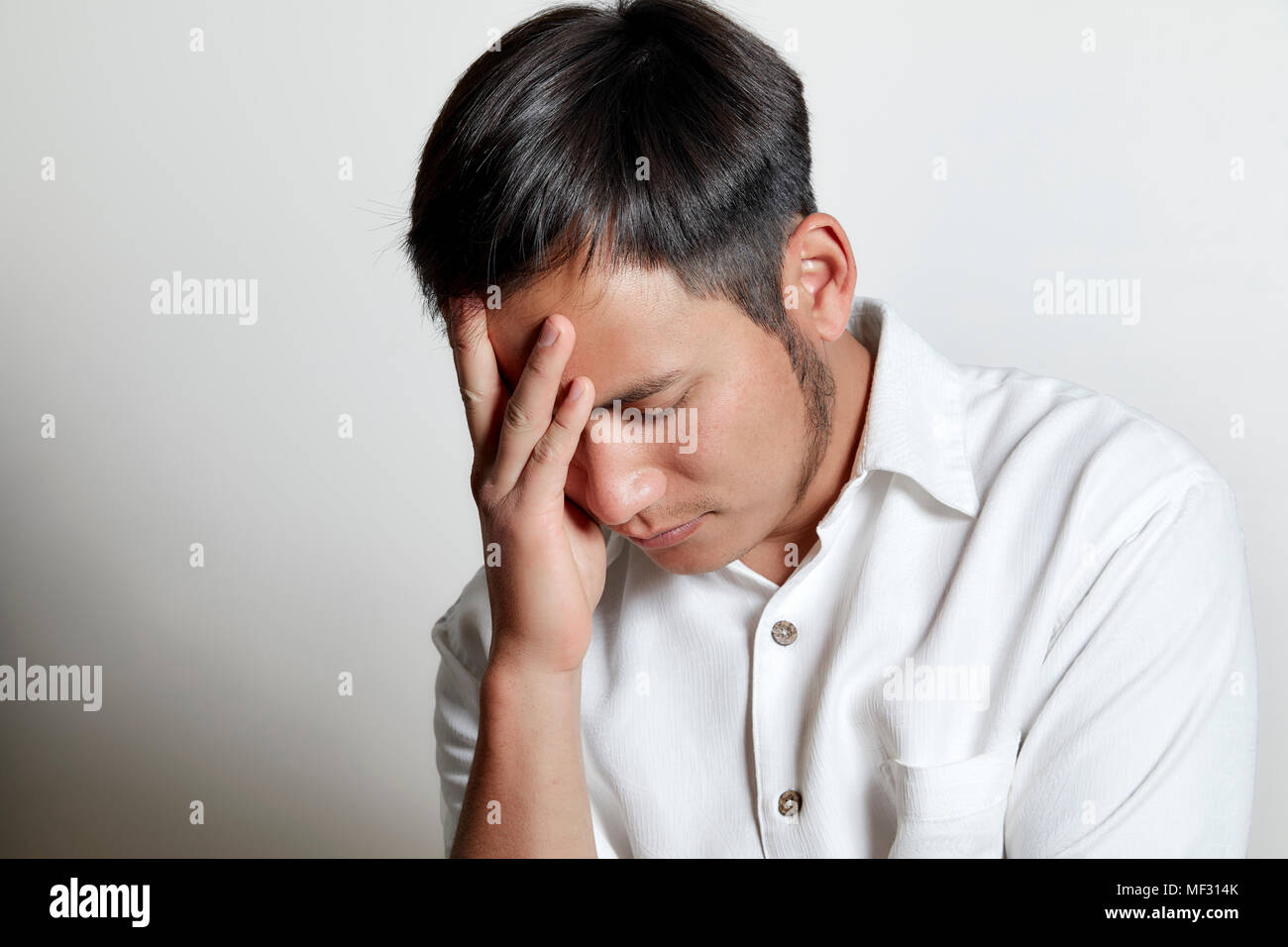 Young Adult man resting his forehead on his hand wearing a white shirt ...