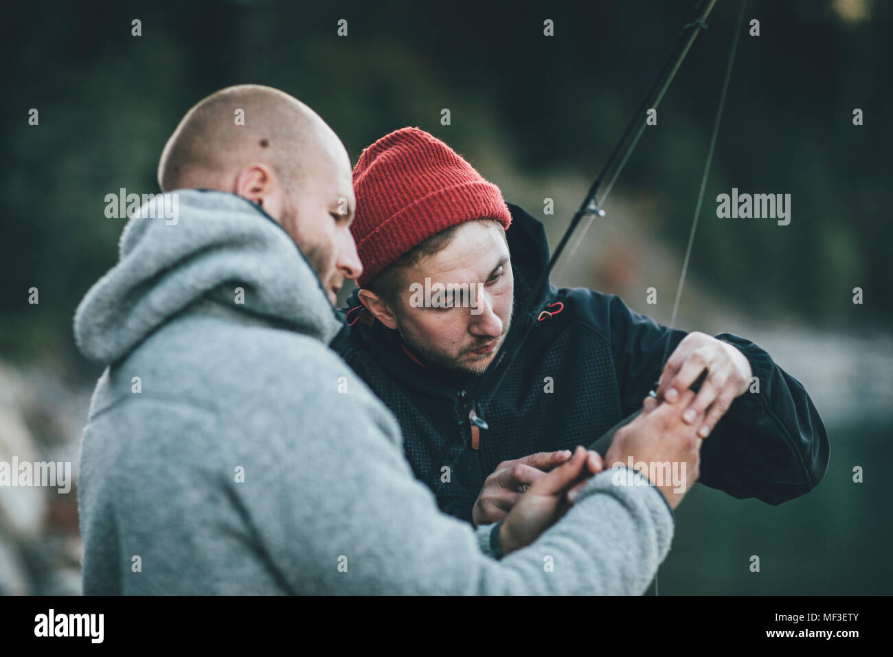 Young man helping friend with fishing rod Stock Photo - Alamy
