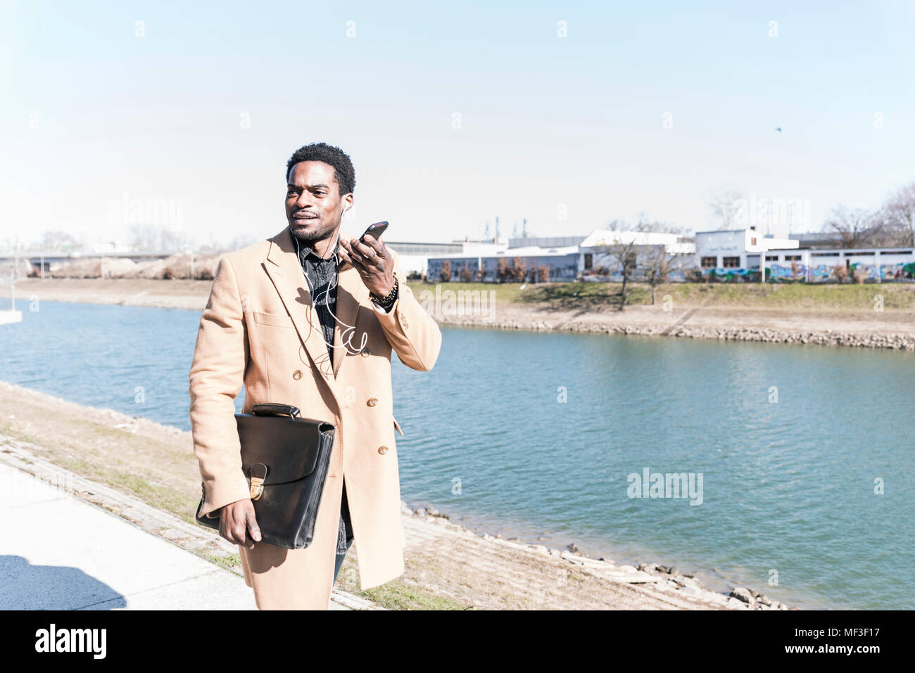 Businessman walking at the waterfront with briefcase, cell phone and ...