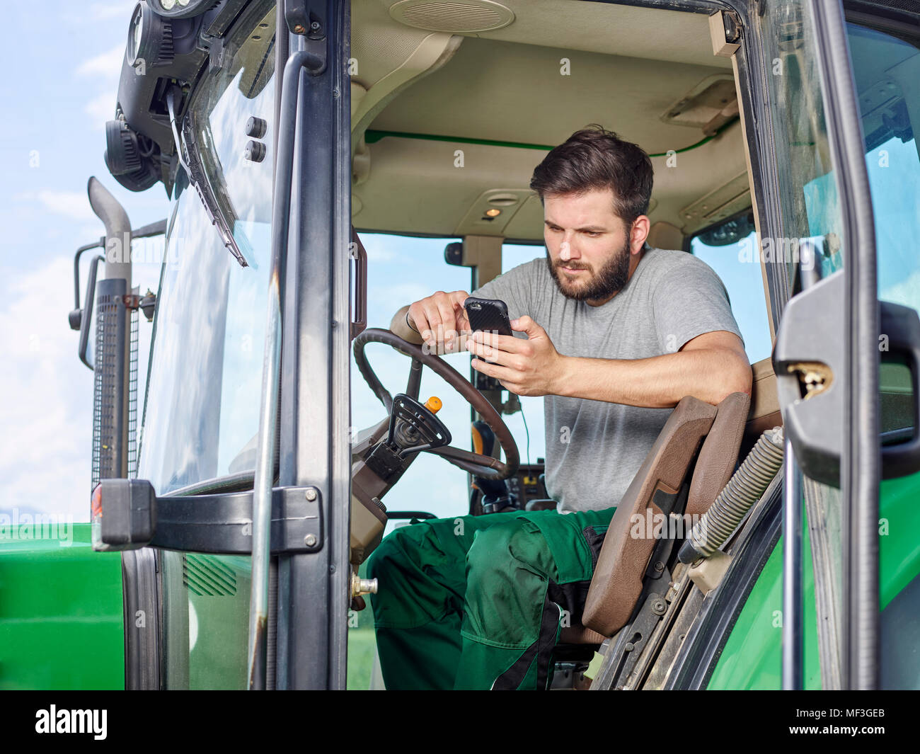 Farmer sitting on tractor using cell phone Stock Photo - Alamy