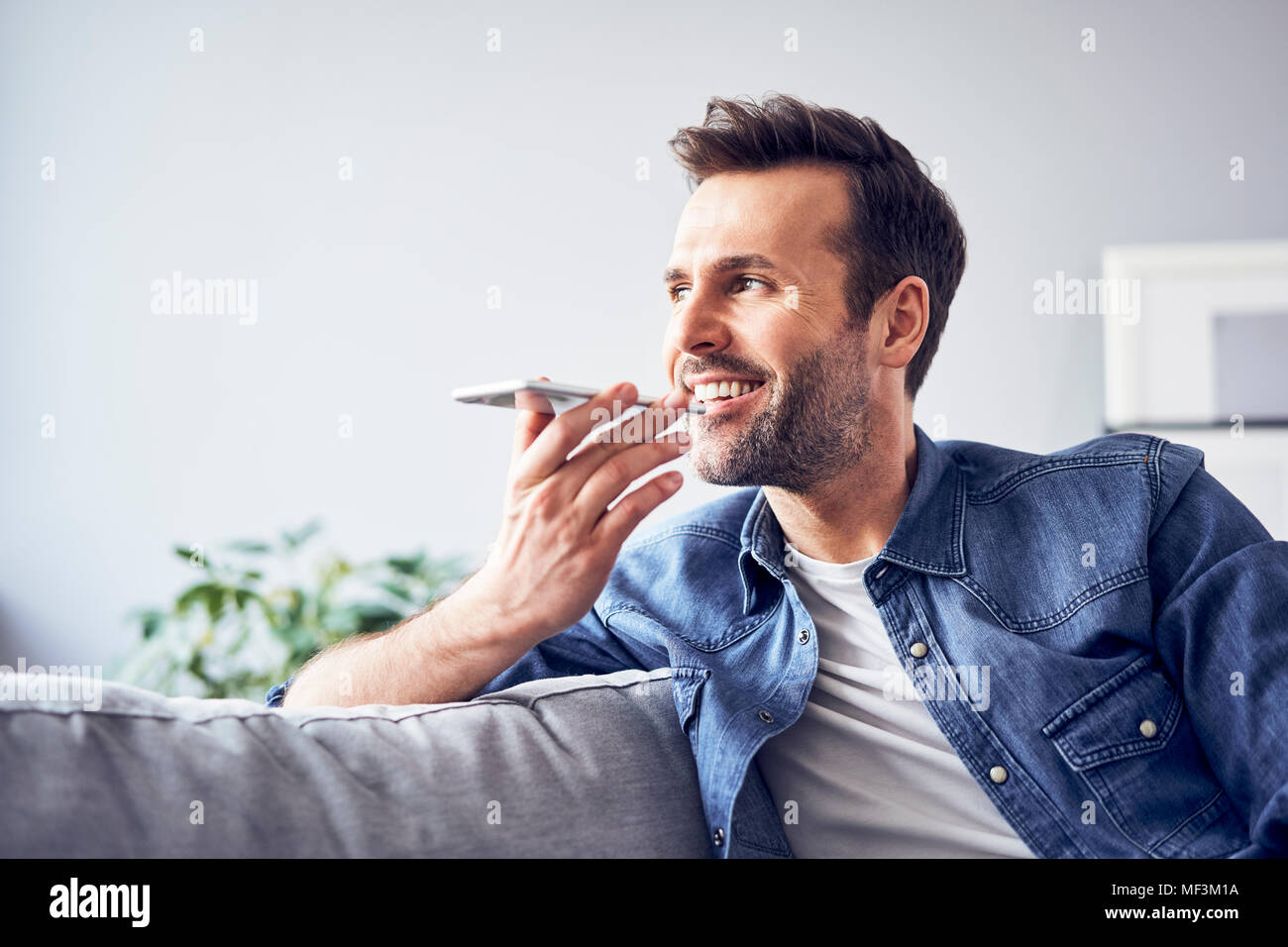 Smiling man sitting on sofa using cell phone Stock Photo - Alamy