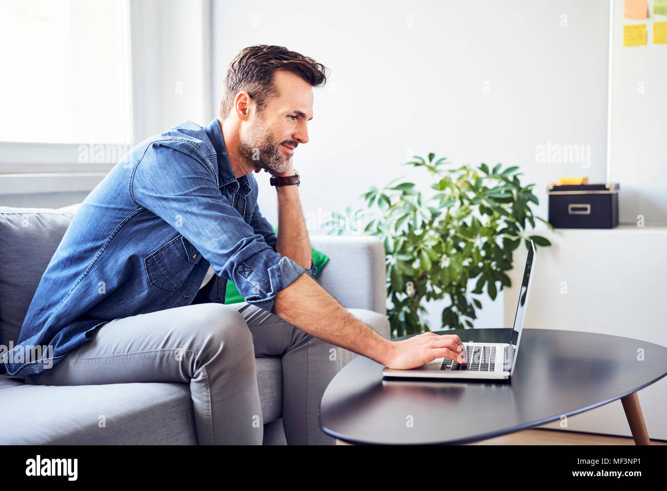 Smiling man sitting on sofa using laptop Stock Photo - Alamy