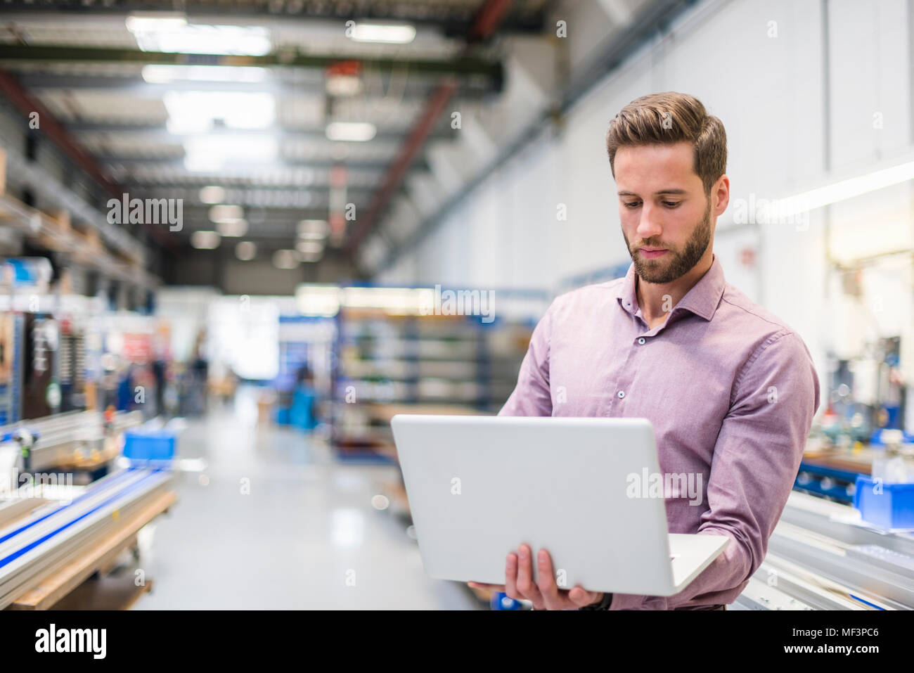 Young businessman using laptop in production hall Stock Photo - Alamy