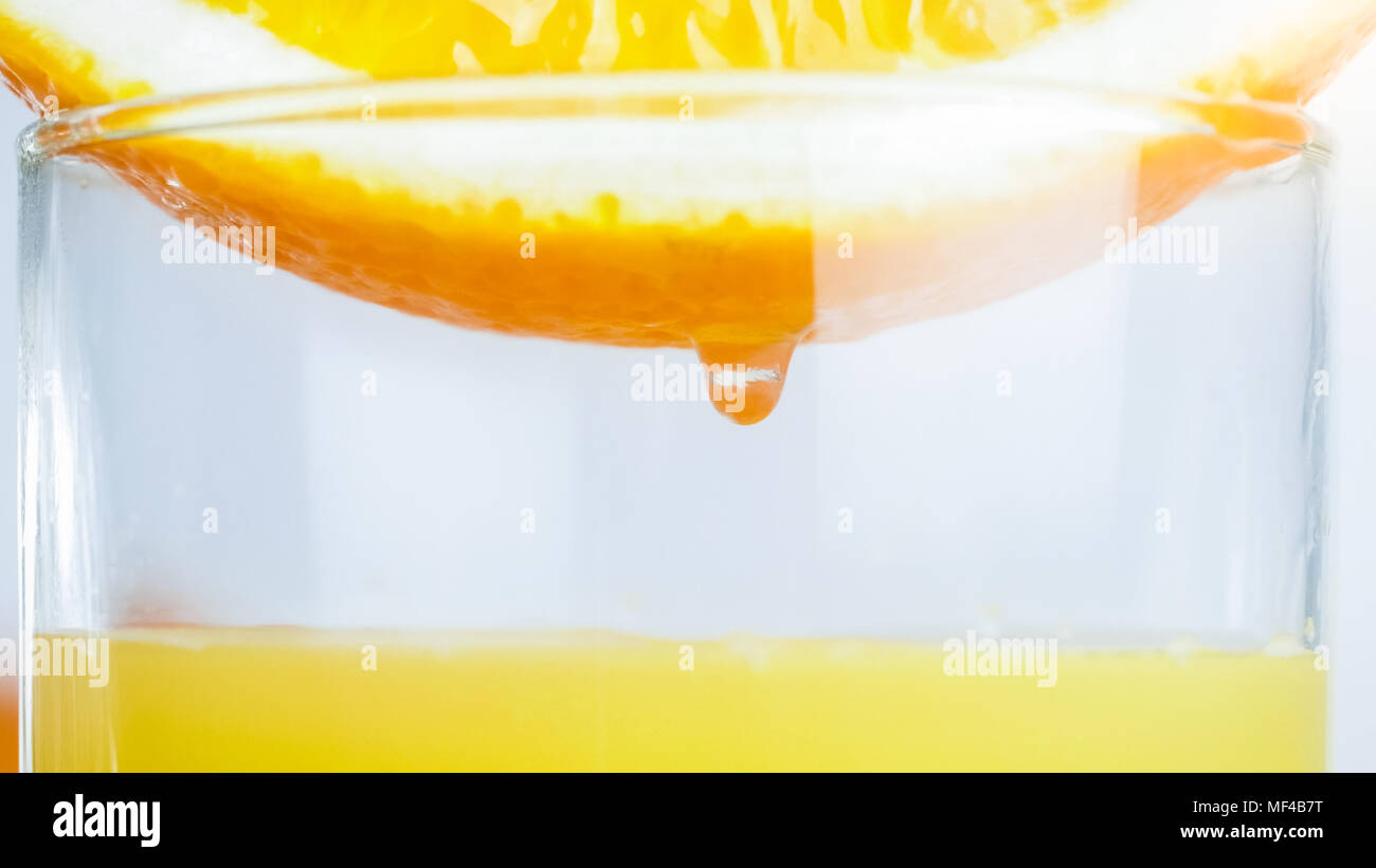 Macro image of juice droplet on side of orange half falling in glass ...