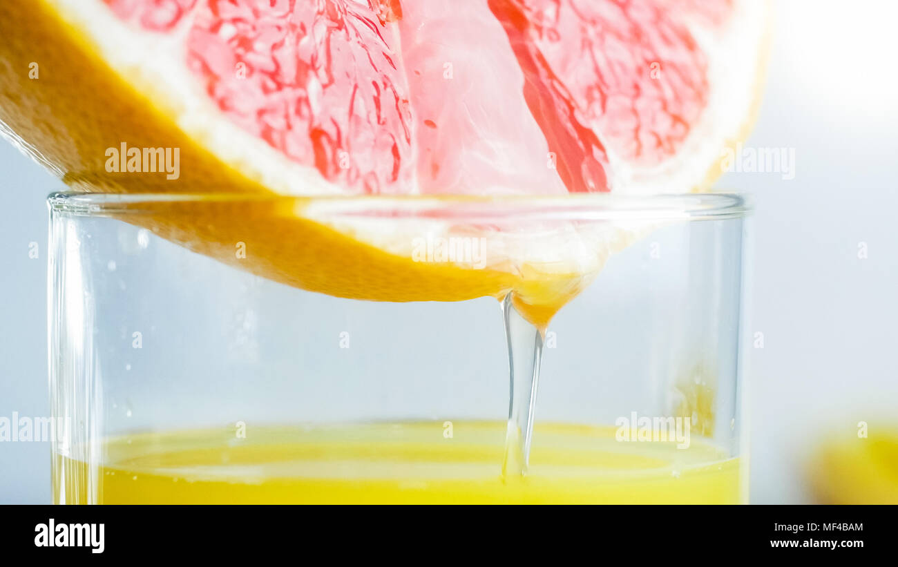 Closeup image of fresh juice dripping from grapefruit slice in glass ...