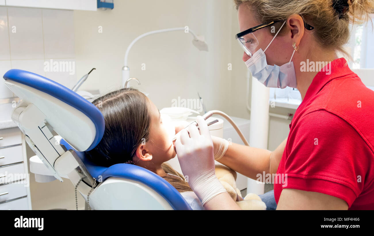 Closeup portrait of female dentist removing caries in girls teeth with ...