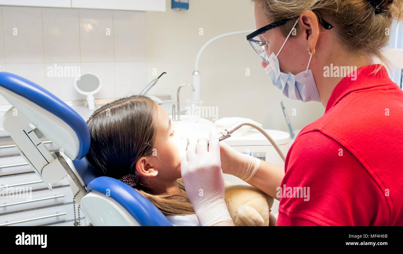 Portrait of female pediatric dentist using dental drill to remove ...