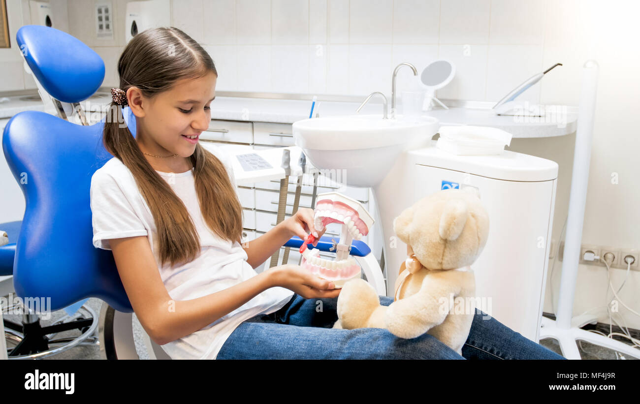 Cute girl sitting in dentist chair and showing her teddy bear how to ...