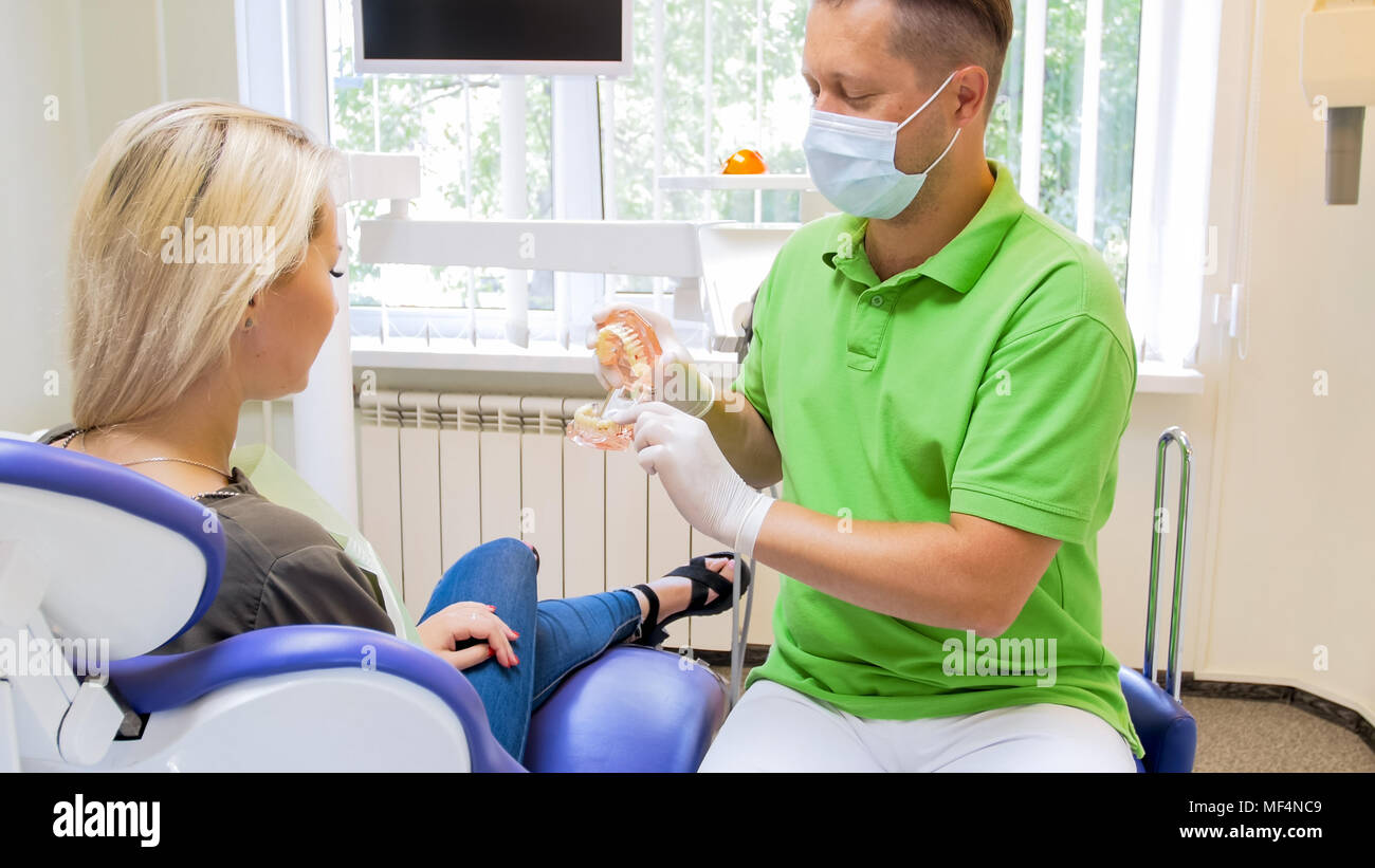 Portrait of male dentist showing plastic teeth model to his patient ...