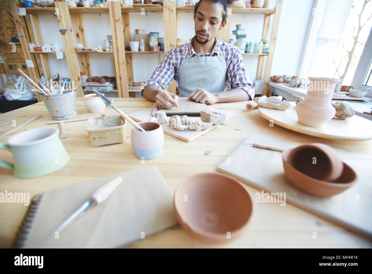 Young mixed race male craftsman writing down new orders in notebook ...