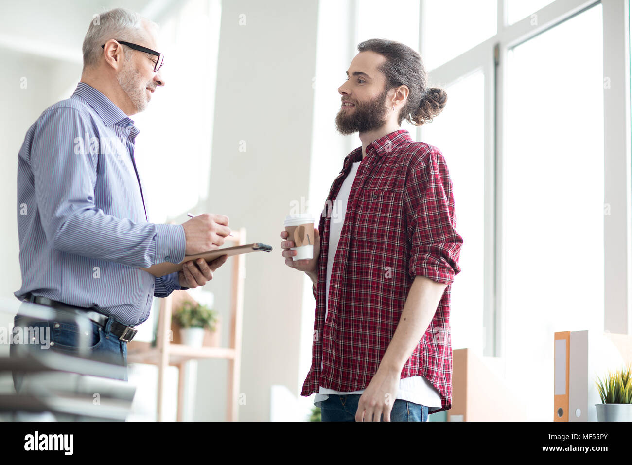 Two colleagues standing and communicating with each other at office ...