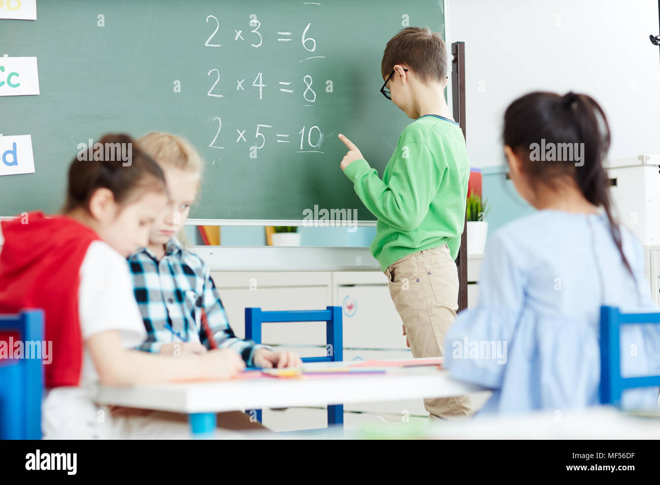 Smart little schoolboy standing by blackboard in classroom and doing ...