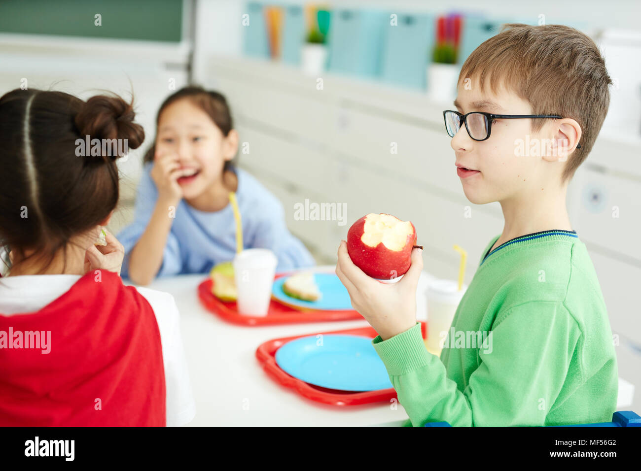 Caucasian boy in glasses eating apple while having lunch with ...