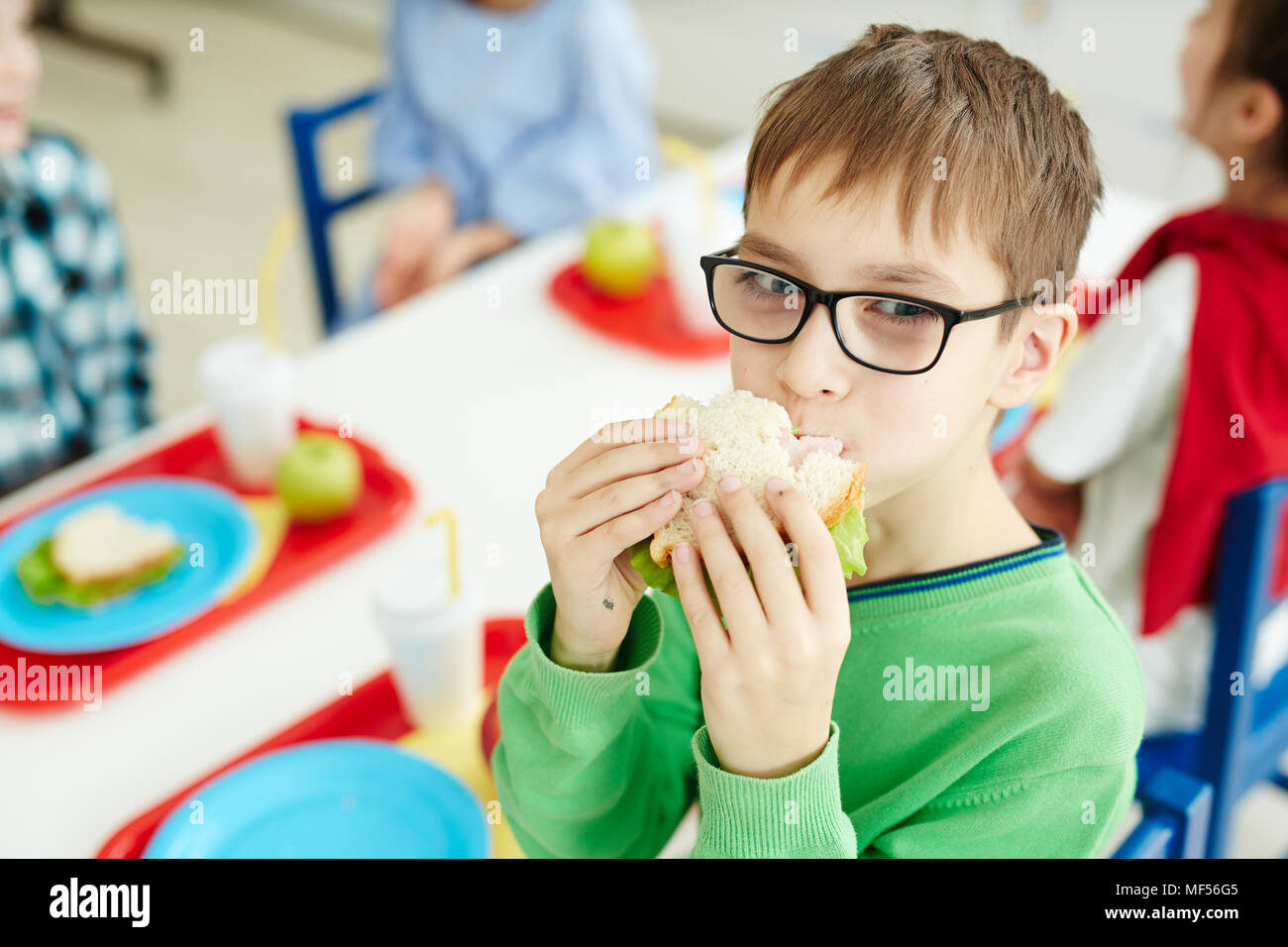 Little Caucasian boy in glasses eating sandwich with appetite while ...