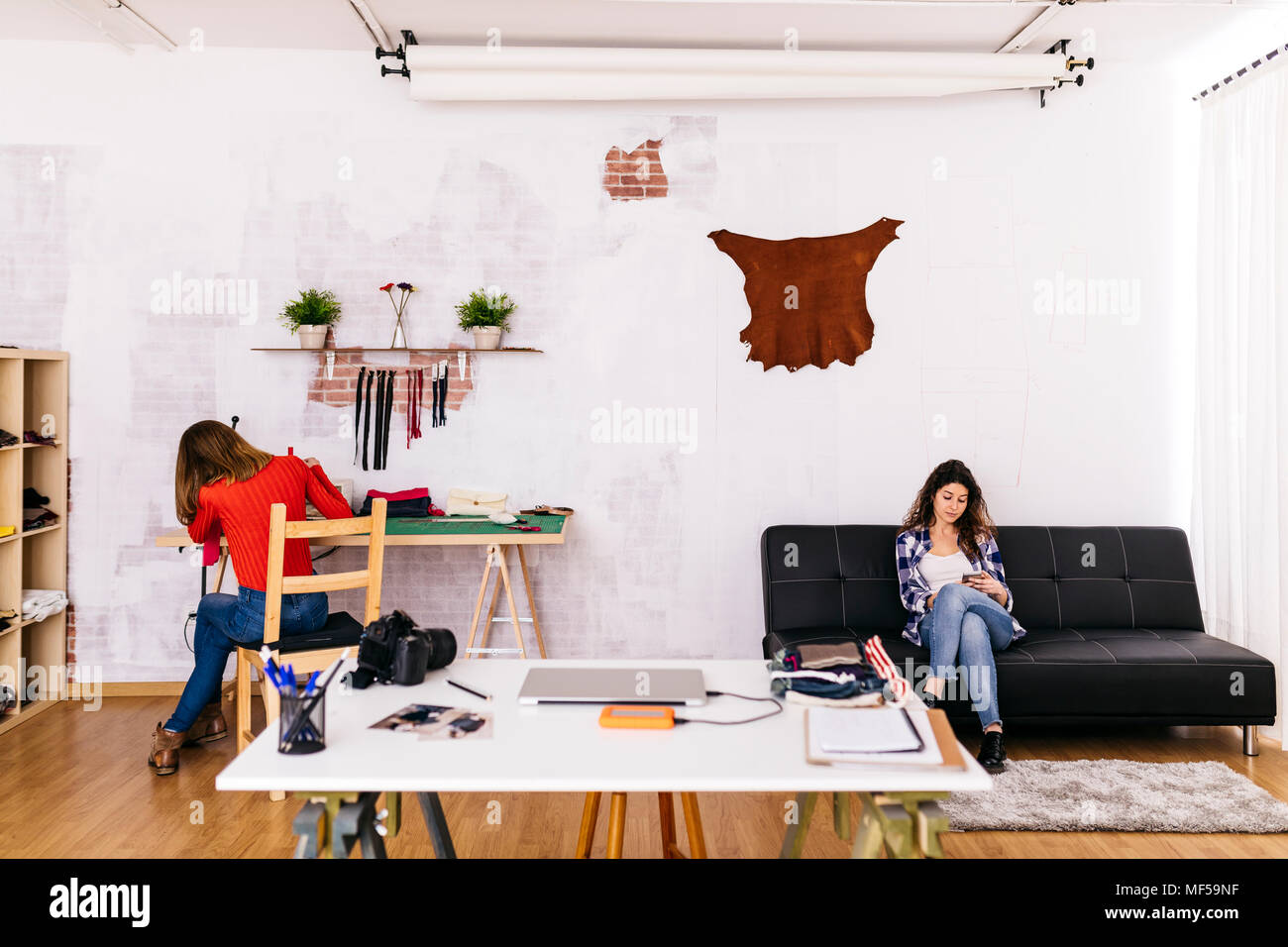 Two women in fashion studio using sewing machine and cell phone Stock ...