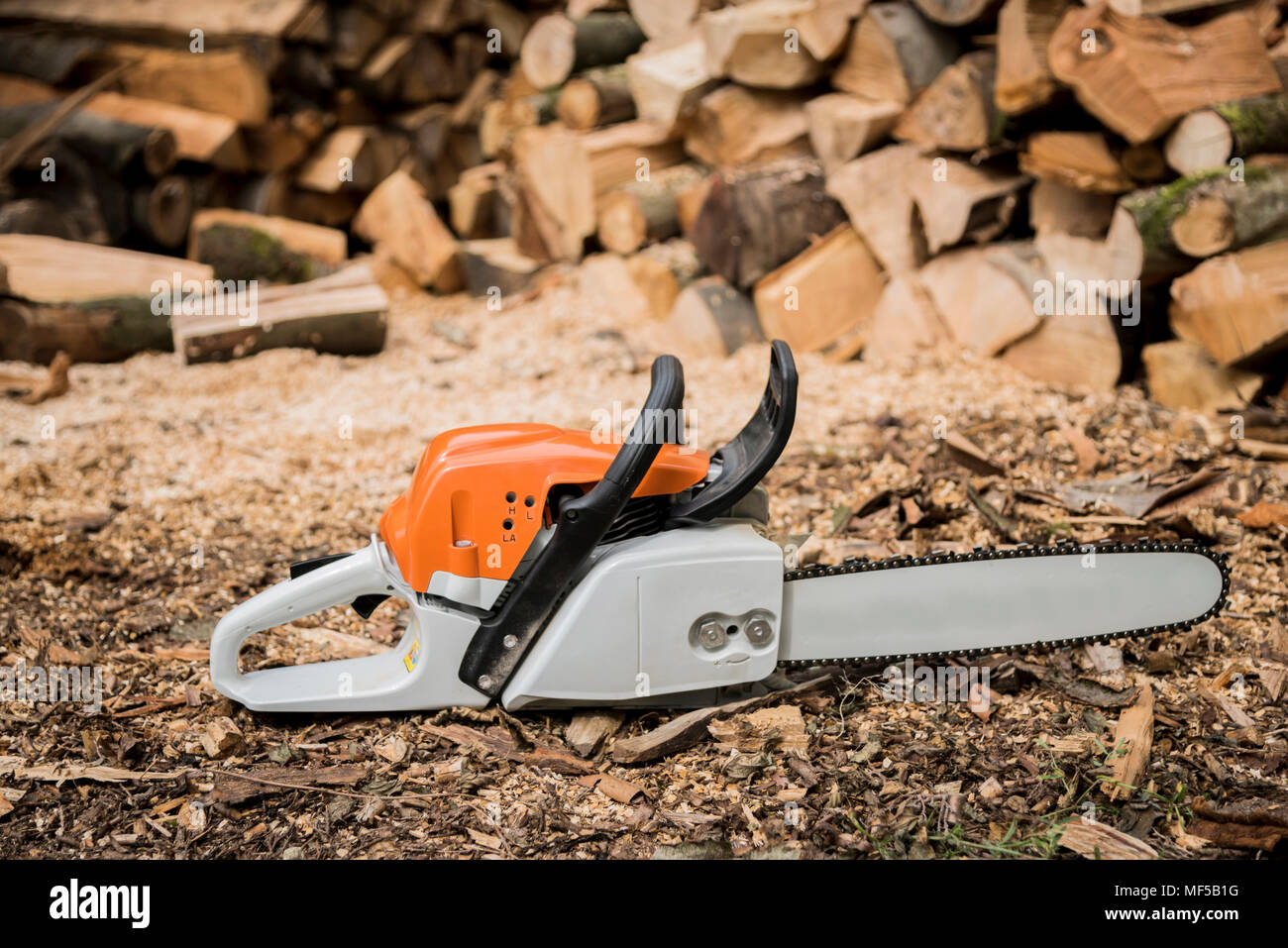 Motor saw on ground in front of stack of wood Stock Photo - Alamy