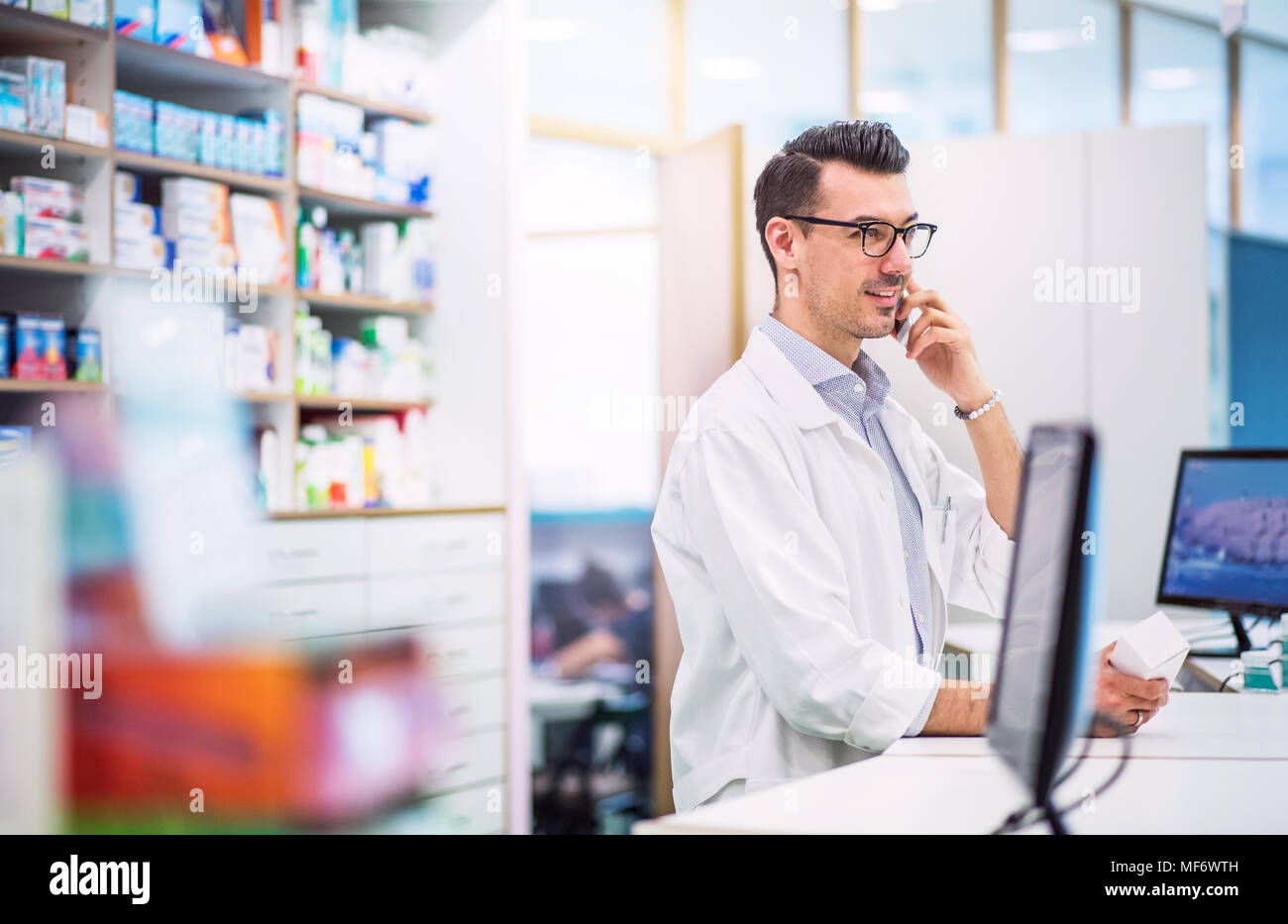 Young friendly male pharmacist with smartphone, making a phone call ...