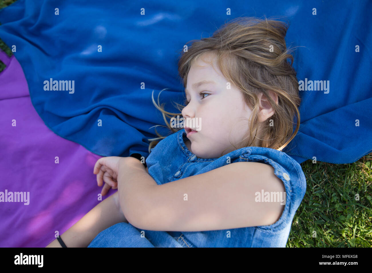 four years old blonde girl lying on towels in the green grass of park ...