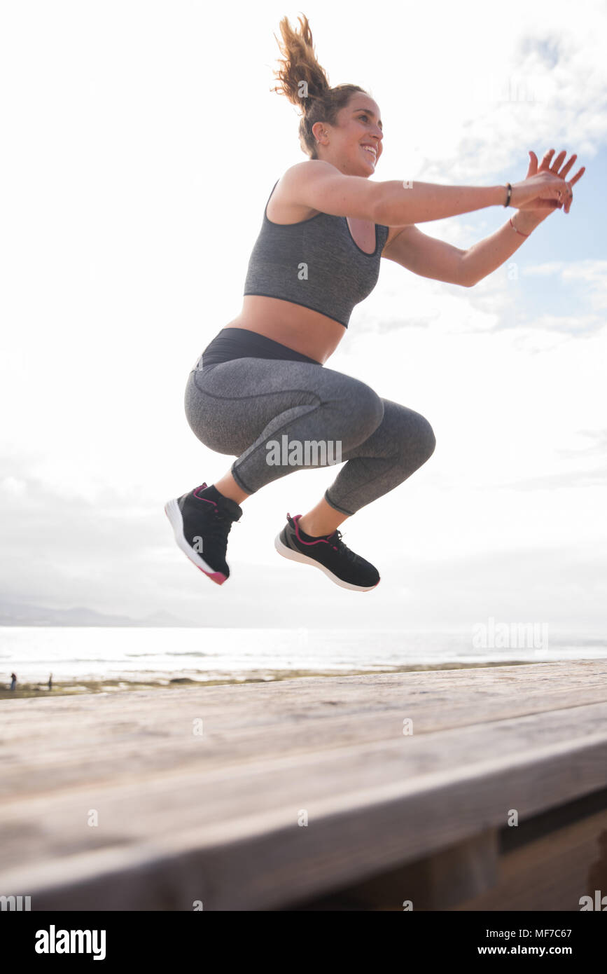Pretty young woman jumping on stairs in high leaps wearing grey fitness ...