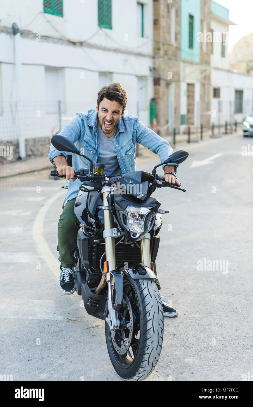 Portrait of screaming young man sitting on motorbike pulling funny ...