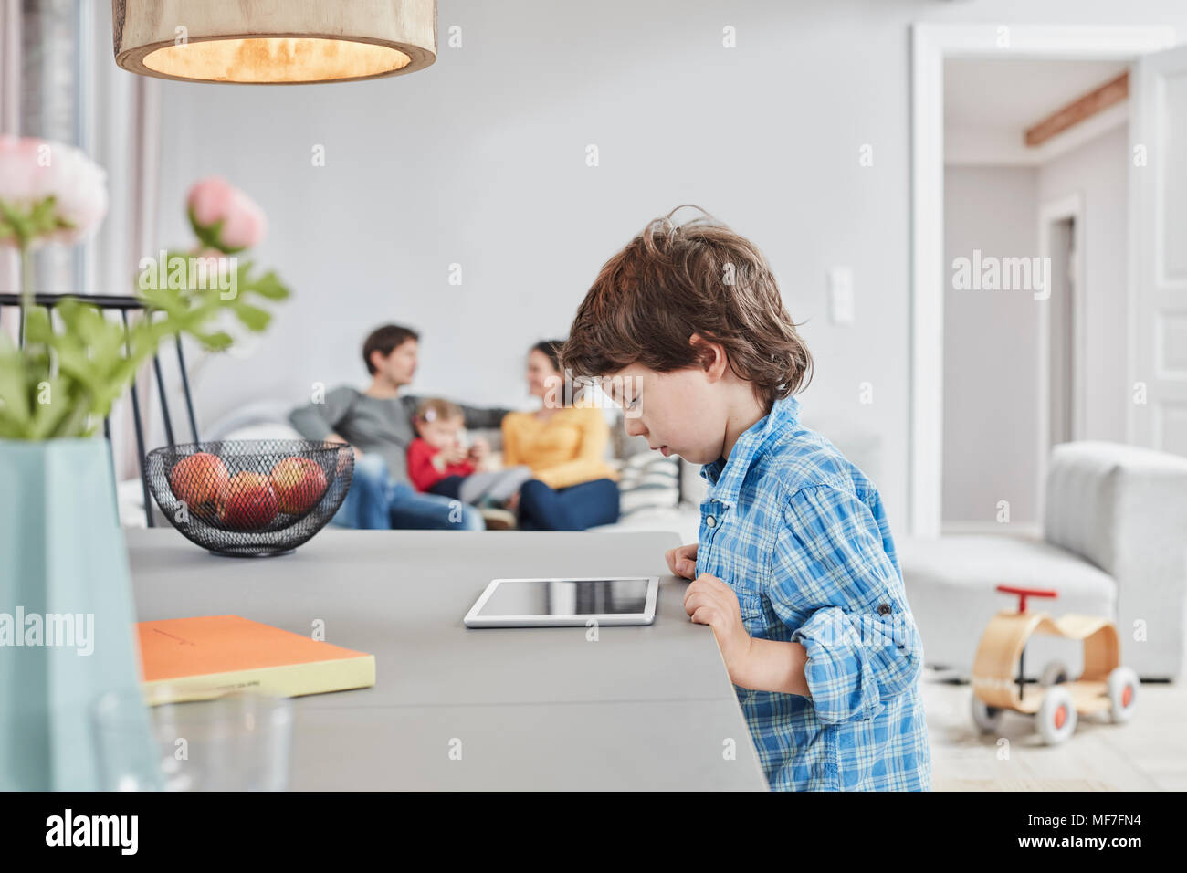 Boy looking at tablet at home with family in background Stock Photo - Alamy