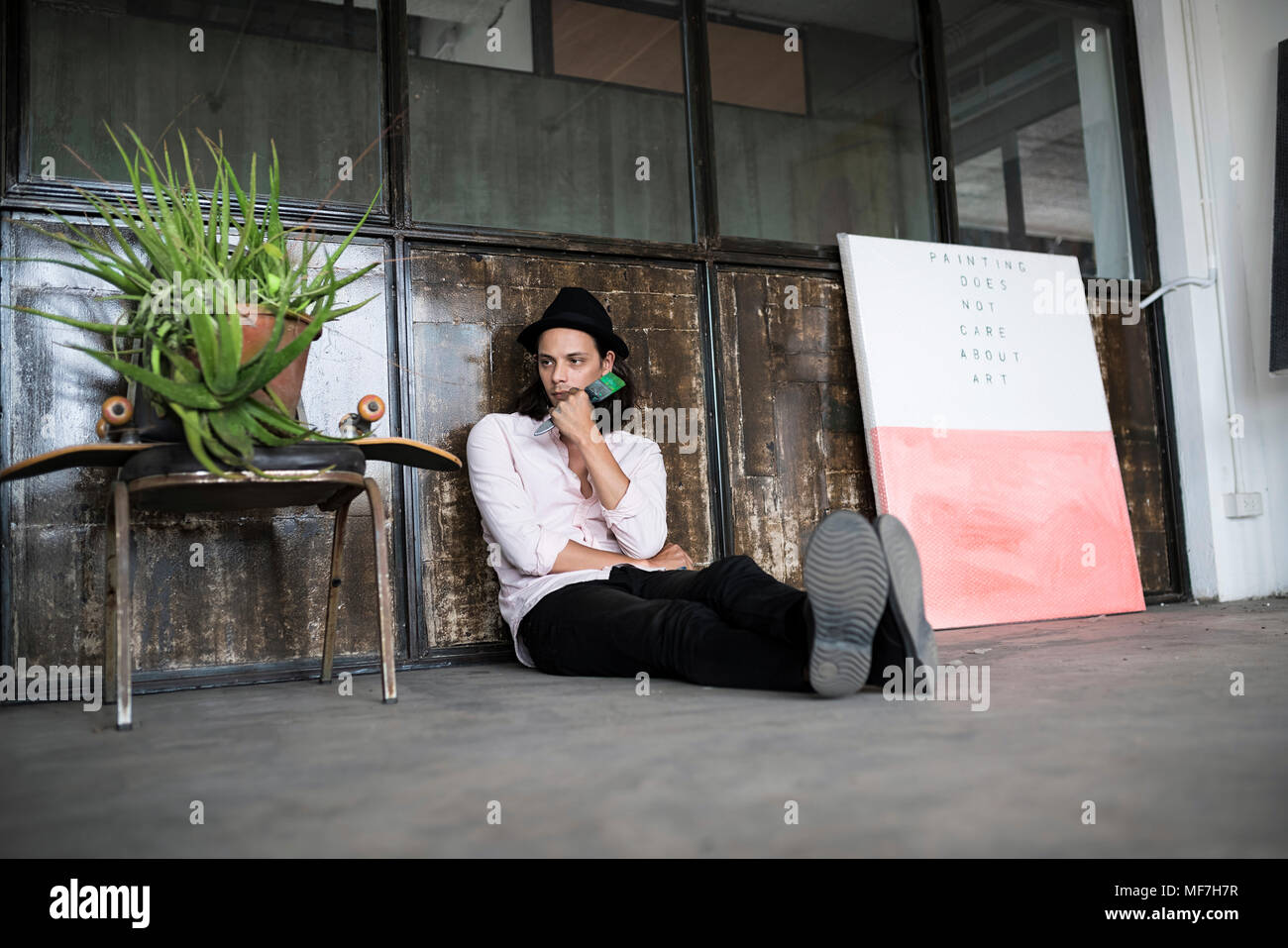 Artist leaning against wall in his loft studio holding a brush with ...