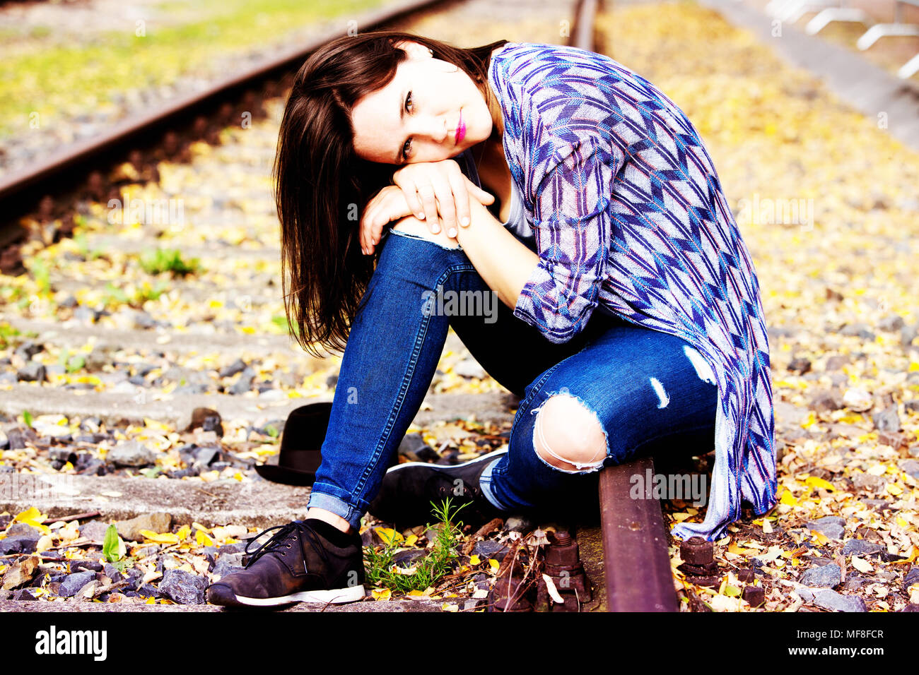 portrait of beautiful young woman sitting on train tracks and looking ...
