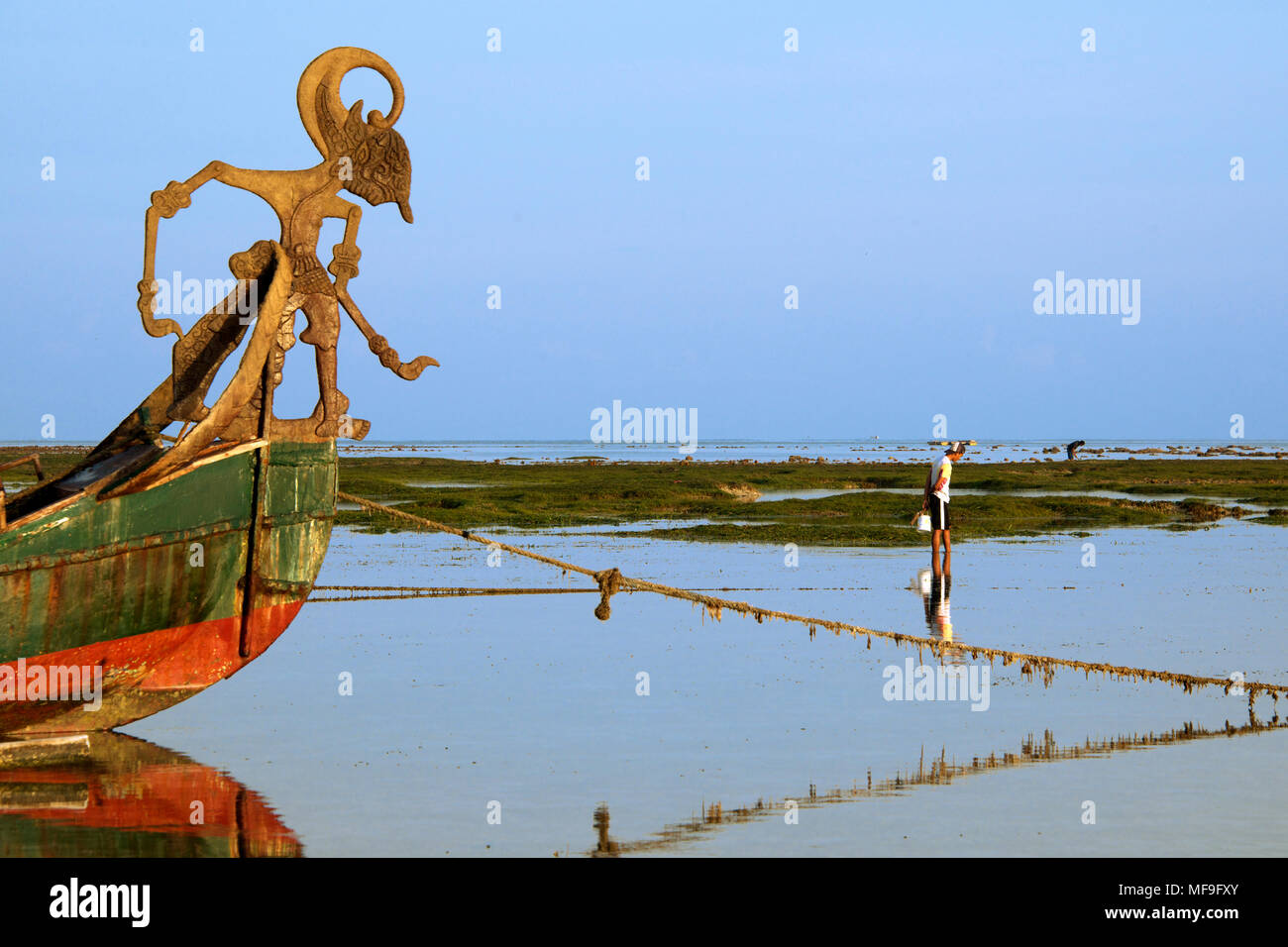 Prow of fishing boat with boy collecting shell fish at low tide in ...