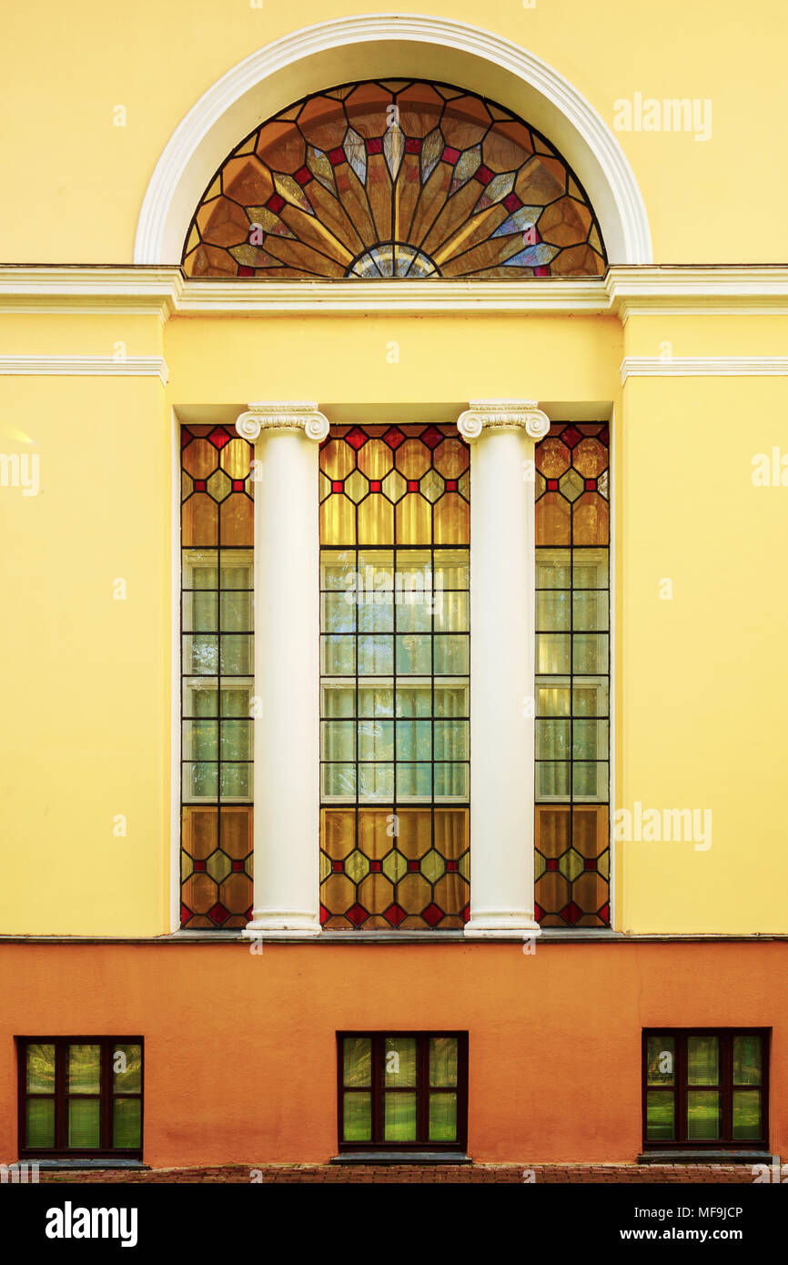 The facade of an ancient building yellow color with stained-glass ...