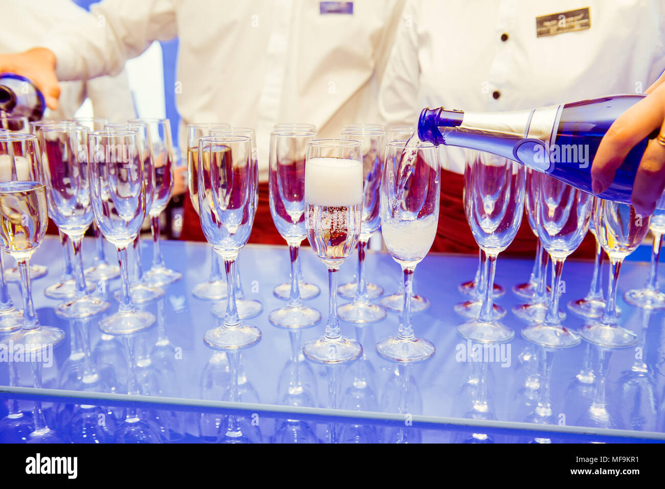 Waiter pouring personal serving Champagne in glasses on bright blue ...