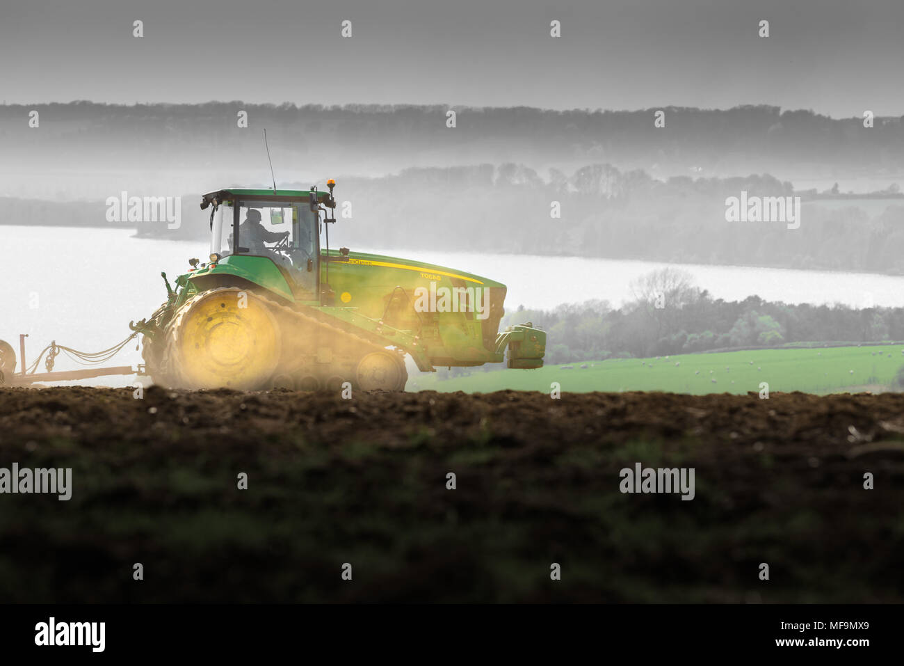A farmer drives his tractor pulling a harrow over ploughed land on a ...