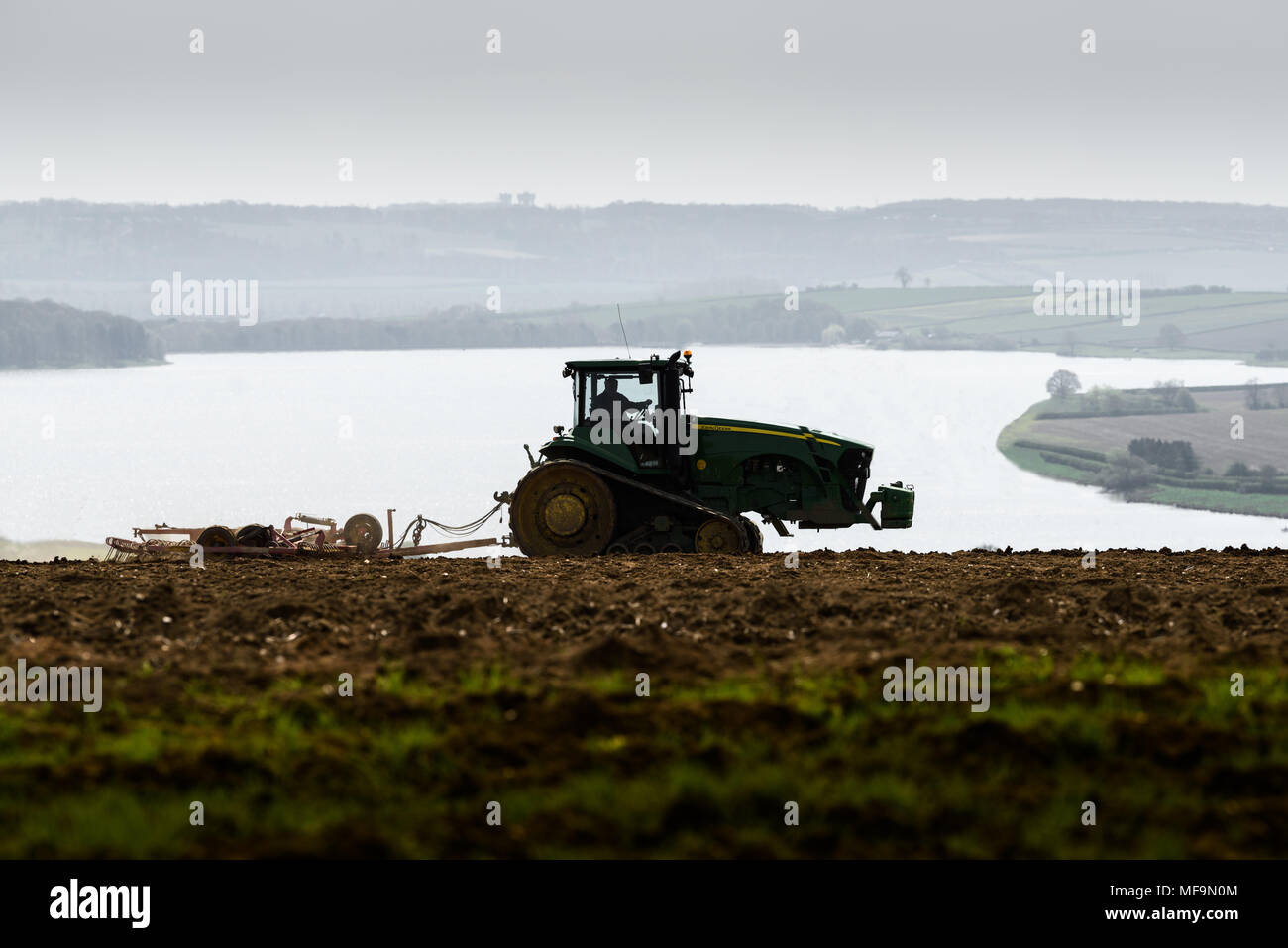 A farmer drives his tractor pulling a harrow over ploughed land on a ...