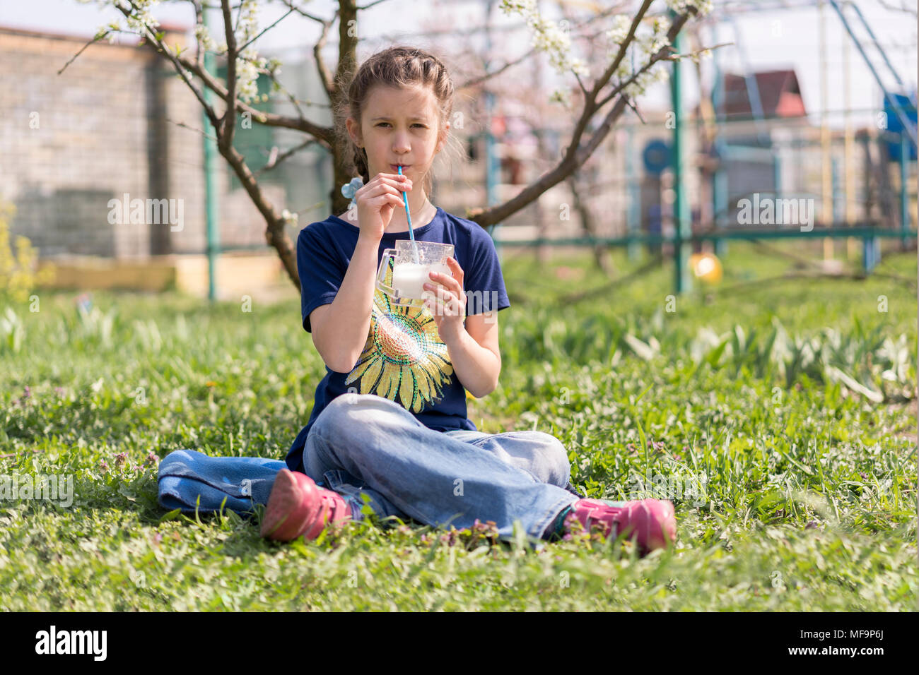 A happy little girl is drinking cappuccino through a straw in a park on ...