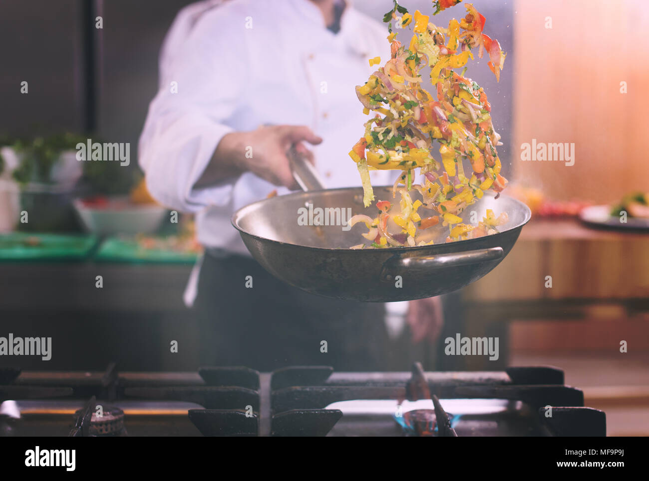 Young male chef flipping vegetables in wok at commercial kitchen Stock ...