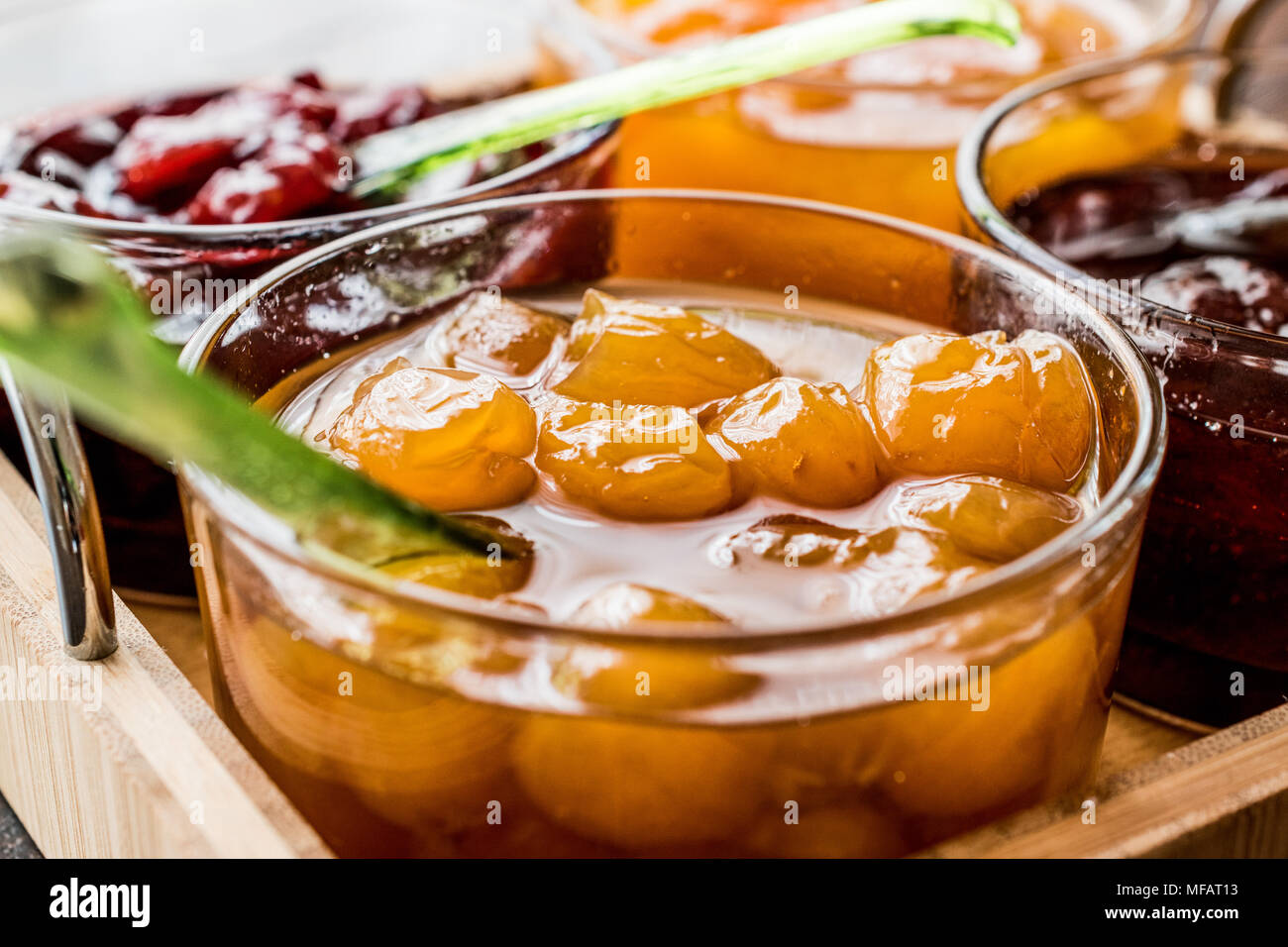 Yellow Plum jam in glass bowl with spoon and various marmalades ...