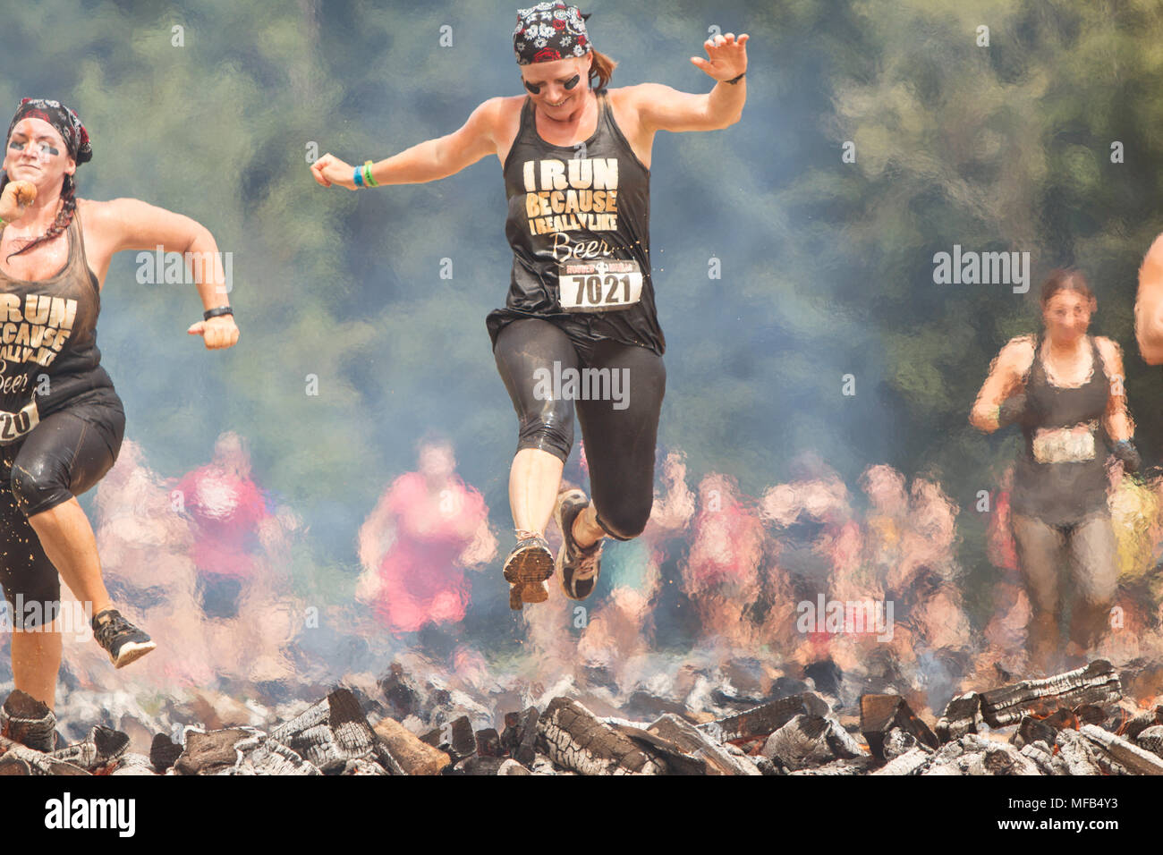 A woman hurdles over burning logs as she competes in the Rugged Maniac ...