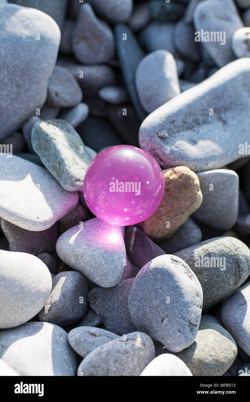 A Pink rubber ball washed up on the shoreline showing beach pollution ...
