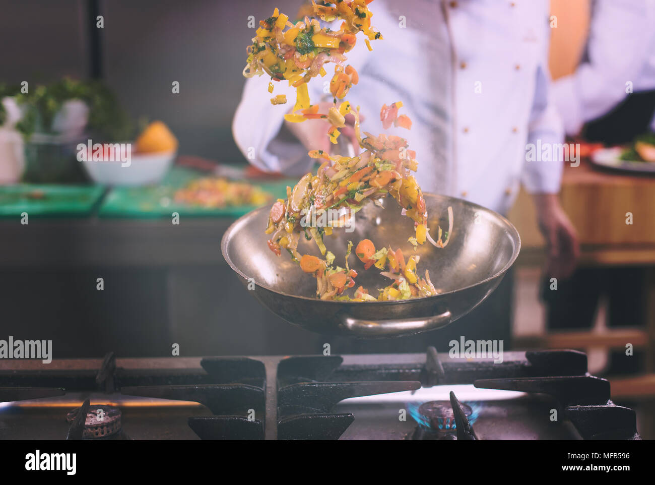 Young male chef flipping vegetables in wok at commercial kitchen Stock ...