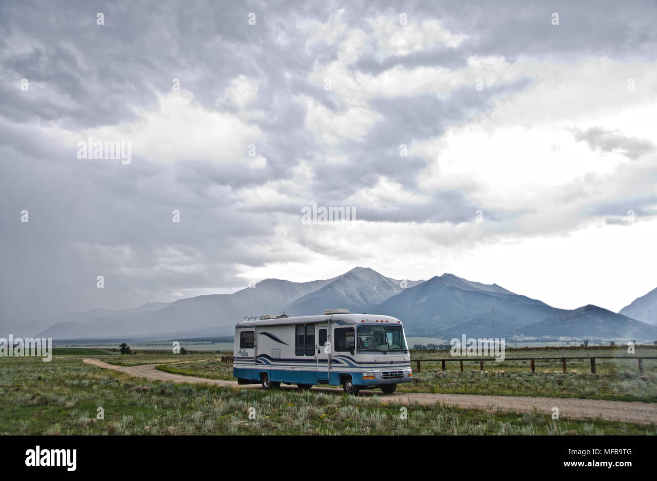 A large Class A motorhome drives down a dirt road at the base of Mount ...