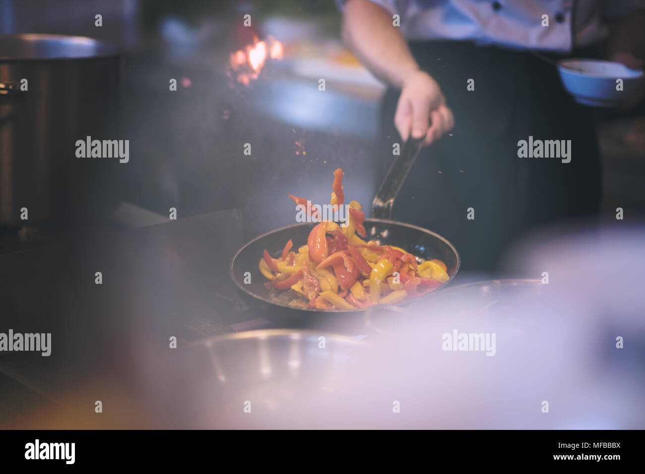 Young male chef flipping vegetables in wok at commercial kitchen Stock ...