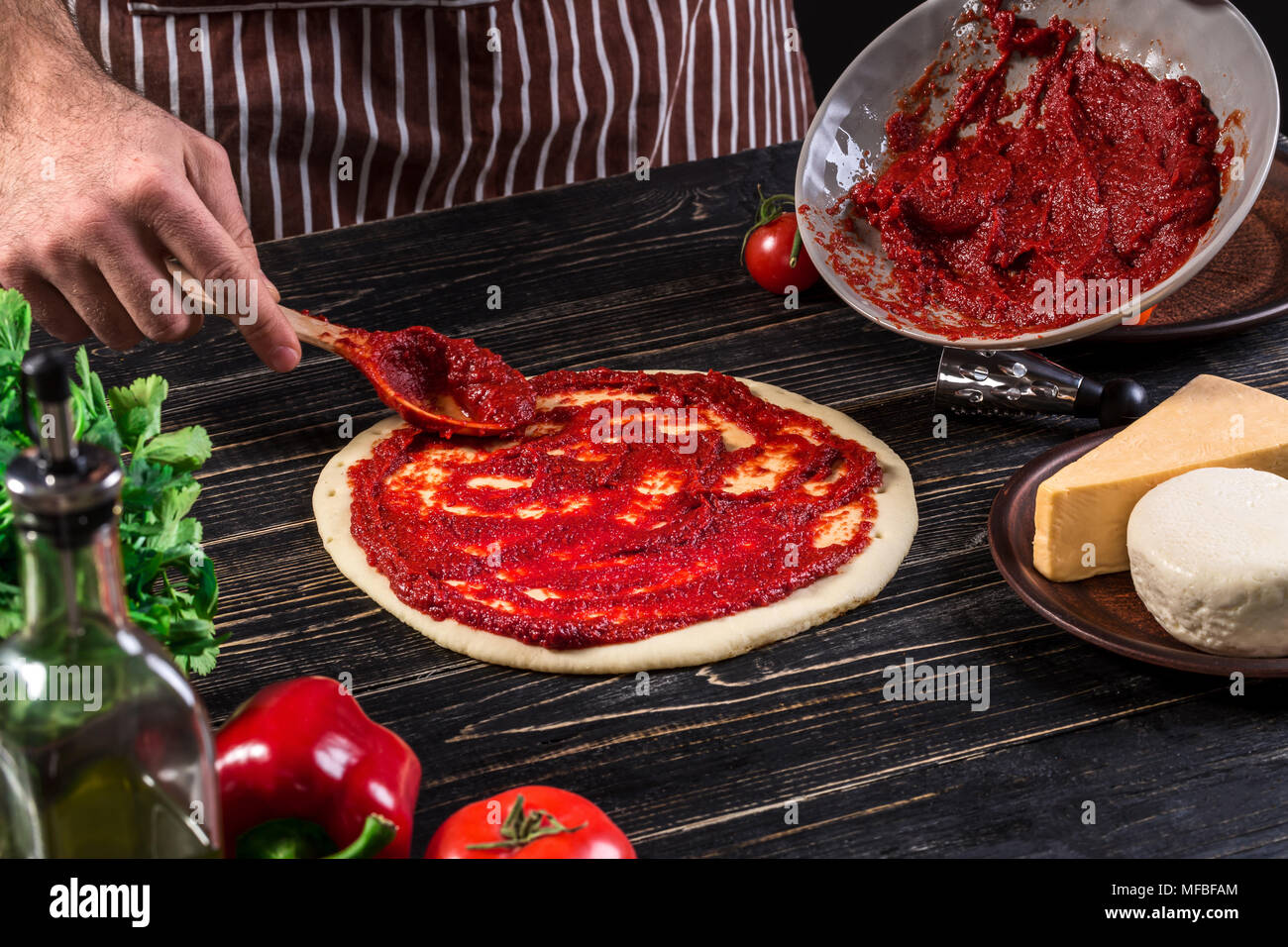 A male hand spreading tomato puree on a pizza base with spoon on an old ...